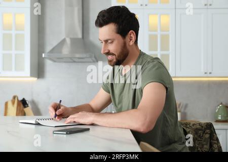 Soldier writing in notebook at white marble table in kitchen. Military ...