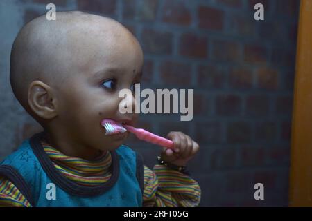18 month old cute bald baby brushes teeth with toothbrush, brick wall ...