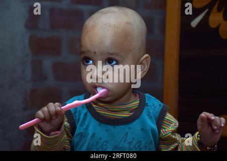 18 month old cute bald baby brushes teeth with toothbrush, brick wall ...
