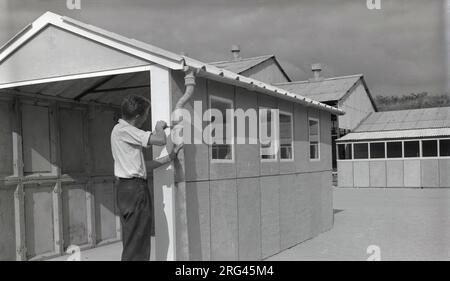 1950s, historical, a man fixing a bracket on the gutter on a prefab ...