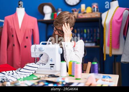Young redhead man tailor stressed using sewing machine at clothing ...