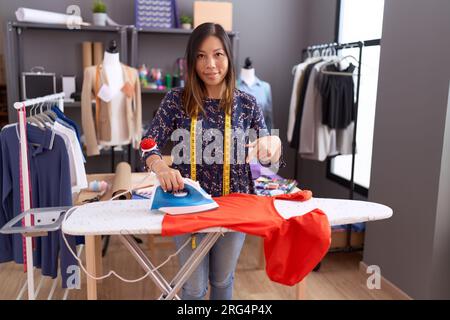 Middle age chinese woman tailor talking on smartphone standing by ...