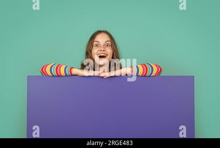shocked child behind blank blue paper with copy space for advertisement ...