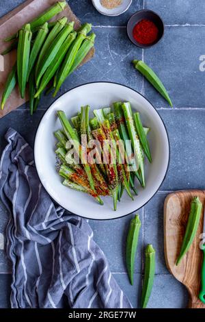 Fresh okra sliced in lengthwise and crosswise on a wooden cutting board ...