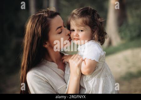 Young mother kissing little daughter lying on grass during sunny day ...