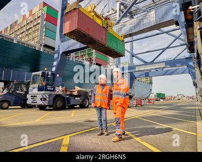 Dock workers by crane lowering cargo container onto truck Stock Photo ...