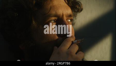 Depressed prisoner in orange uniform sits on bed, smokes cigarette in ...
