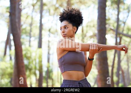 Serious multi-ethnic woman stretches arms before trail run in forest ...