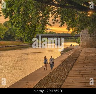People walk down the embankment of a river to take a boat ride across ...