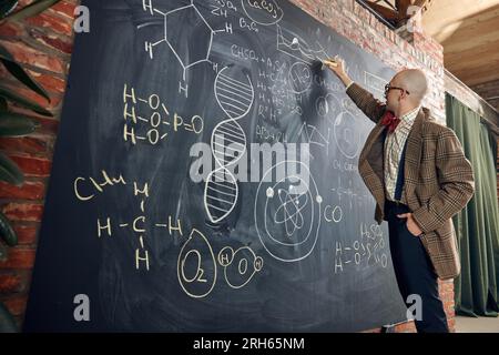 Young bald man, scientist, professor standing by blackboard with ...
