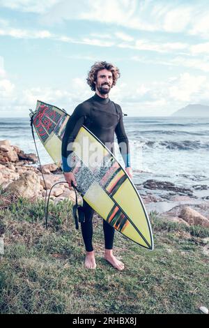 Fit young surfer man with curly blond hair with surfboard goes by the ...