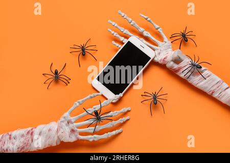 Skeleton hands with modern mobile phone, skulls and spiders for ...
