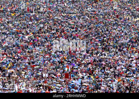 A dense, colorful crowd with umbrellas stands with unrecognisable faces ...