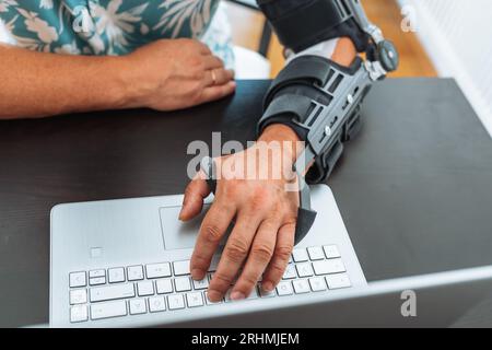 Man with adjustable articulated elbow orthosis typing on laptop ...