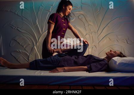 Masseuse stretching client lower limb muscles during Thai massage ...