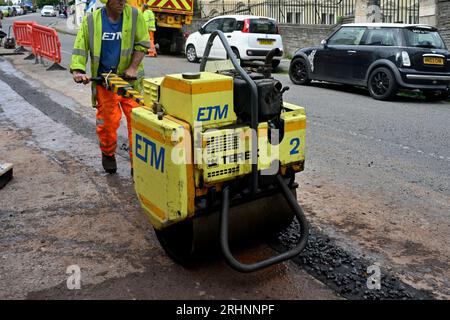 Workmen laying asphalt and compacting with vibrating roller finishing ...
