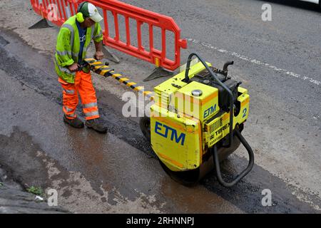 Workmen laying asphalt and compacting with vibrating roller finishing ...