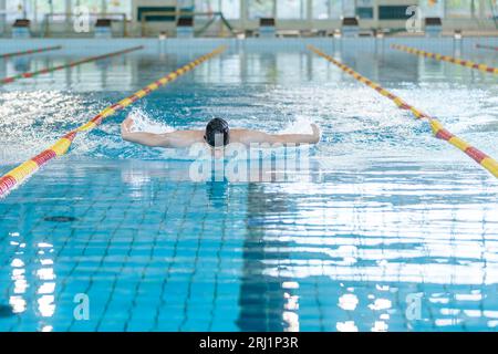 Professional male swimmer performing butterfly style in the indoor lap ...