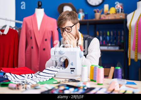 Young redhead man tailor stressed using sewing machine at clothing ...
