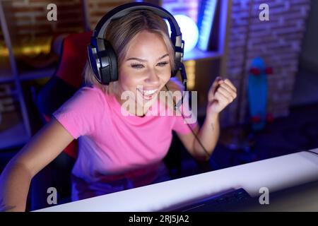 Young blonde woman streamer playing video game using computer at gaming ...