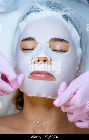 Professional doctor cosmetologist applying sheet mask on face of ...