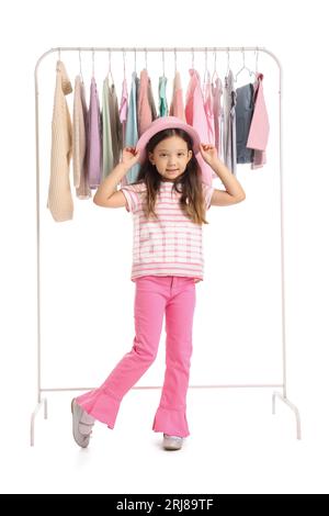 Cute little girl near rack with stylish clothes on light background ...