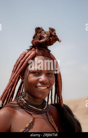 A Himba woman adorned in traditional attire and jewelry stands in a ...