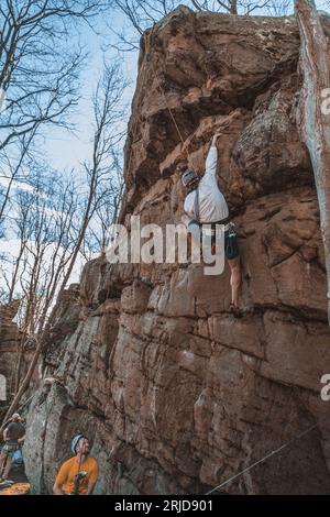 Rock climbers scaling a rugged cliff face with trees and cloudy sky in ...