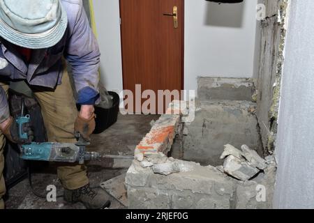 A bricklayer uses a jackhammer to break a wall in a house while ...