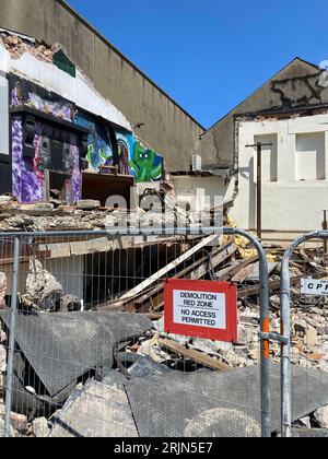 A demolition zone sign on a metal fence with stone debris in the ...