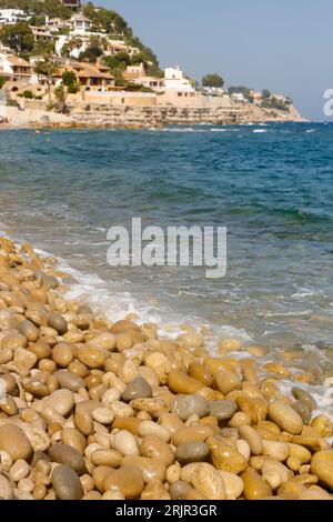 A sun-drenched beach in Alicante, Spain, featuring textured sea rocks ...