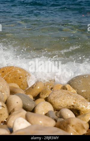 A sun-drenched beach in Alicante, Spain, featuring textured sea rocks ...
