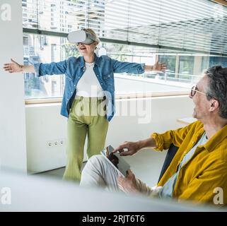 Happy businessman with colleague wearing virtual reality simulator ...