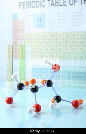 Molecular model on light surface against periodic table, space for text ...