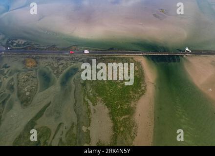 Vehicles travel along Holy Island causeway in Northumberland which ...