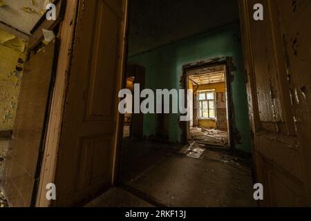 Corridor with white and green shabby walls and big doorways inside old abandoned destroyed ...
