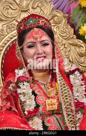 A happy smiling Nepali bride iwearing a red saree and gold jewelry ...