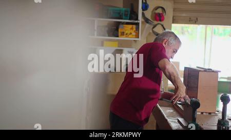 Older man working at workshop, grabbing tools from wall and engaged ...