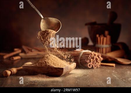 Cinnamon powder is poured into a wooden bowl. In the background are ...