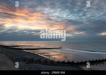 Cloudy sunset over Sheringham breach, peaceful walkers on the shore ...