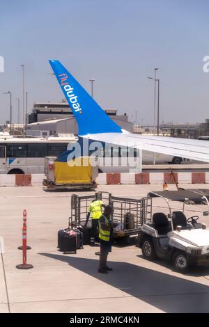 Airport workers load baggage into a luggage vehicle from an airplane ...