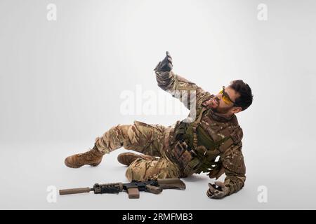 Weak fallen soldier in camouflage asking for help indoors. Side view of ...