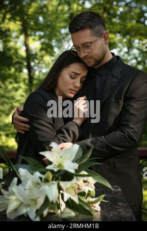 Sad couple mourning near granite tombstone with white lilies at ...