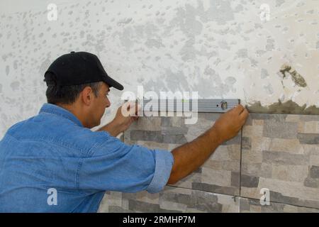 Image of a tiler who uses a spirit level to check and ensure that the ...