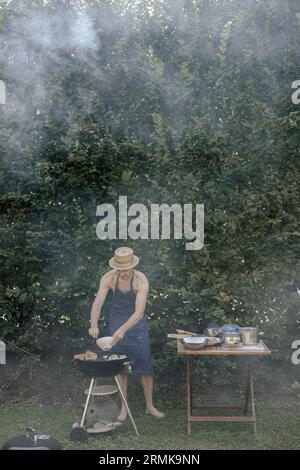 Middle aged Caucasian man grilling meat on open flame using tongs ...