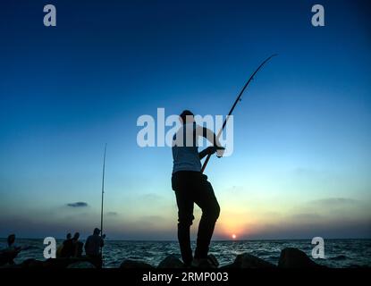 Palestinian men use fishing rods to catch fish during sunset on the ...