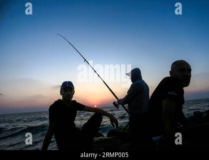 Palestinian men use fishing rods to catch fish during sunset on the ...
