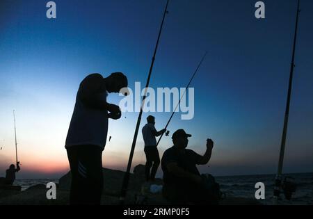 Palestinian men use fishing rods to catch fish during sunset on the ...