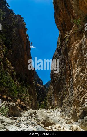 Towering vertical cliffs and a rocky, dry riverbed in the Samaria Gorge ...