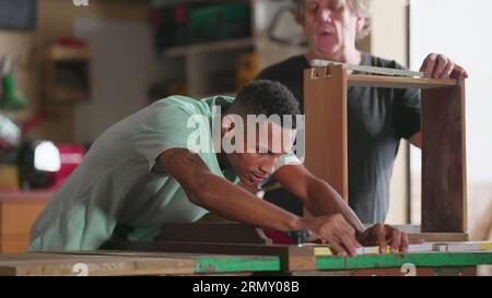Candid scene of carpenters working at workshop, a young black pupil ...